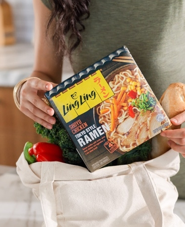 Woman holding a package of Ling Ling shoyu chicken ramen