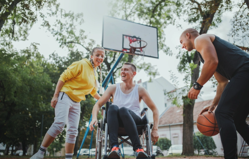 Three people playing basketball outdoors, with one player in a wheelchair