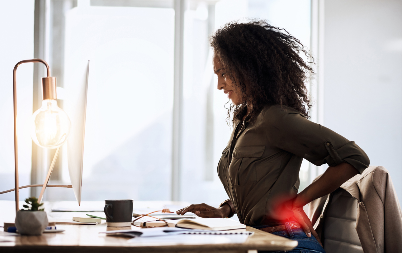 Woman with lower back pain while sitting at her desk (credit - Haraman)